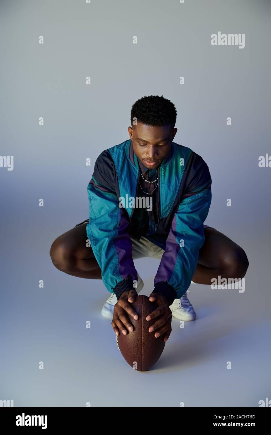 A stylish young African American man crouching down with a football in ...