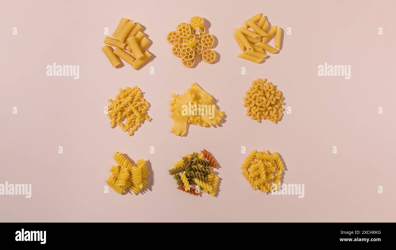 Assorted uncooked pasta varieties arranged on a pink background ...