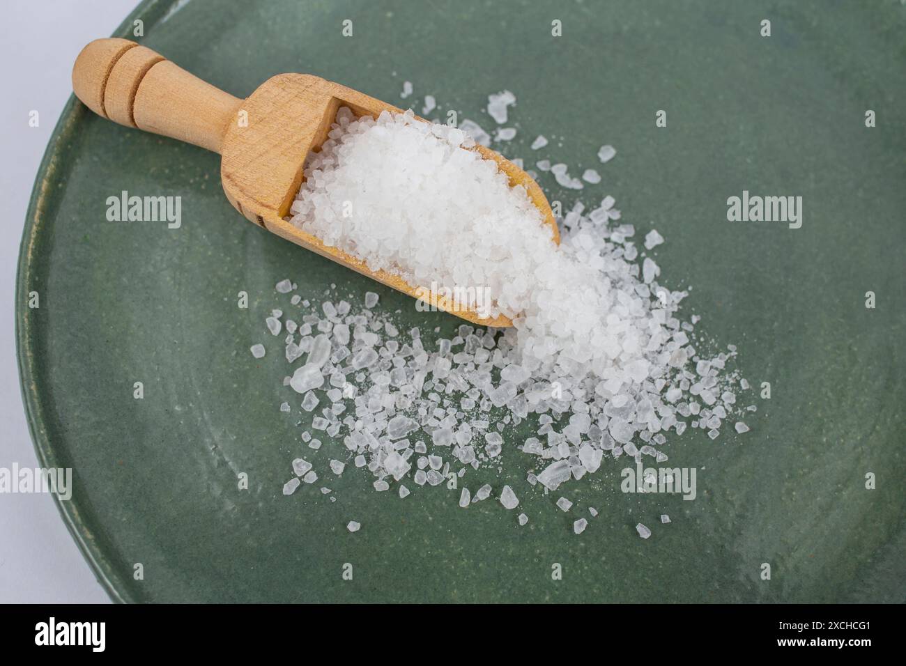Wooden scoop full of sea salt on a green ceramic plate, soft focus ...