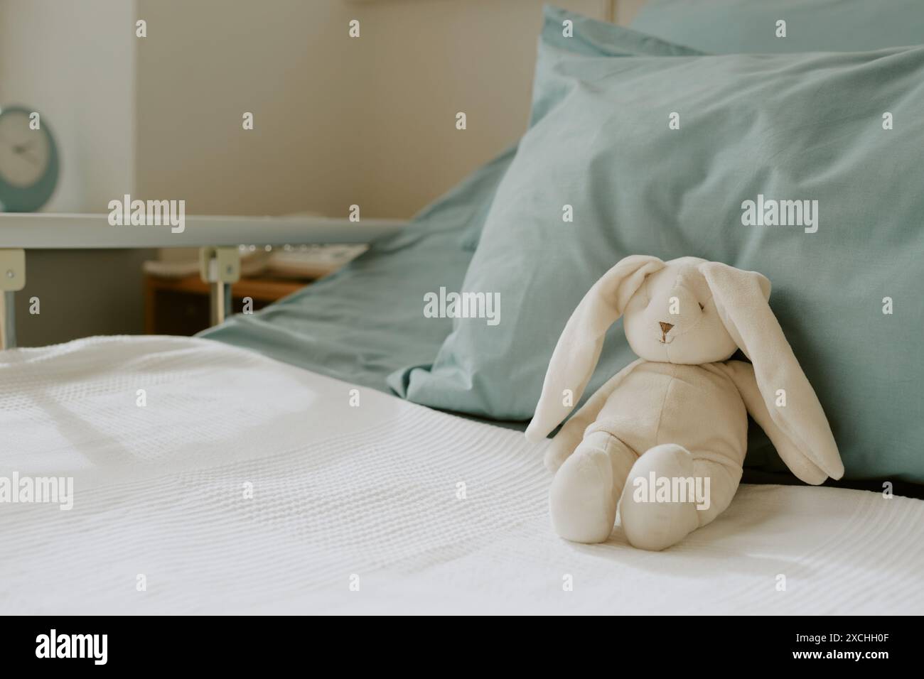 Fluffy plush bunny sitting on hospital bed with mint linen and white ...