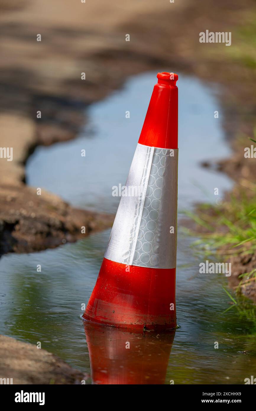 Deep pot hole in a country lane filled with water and marked with a ...