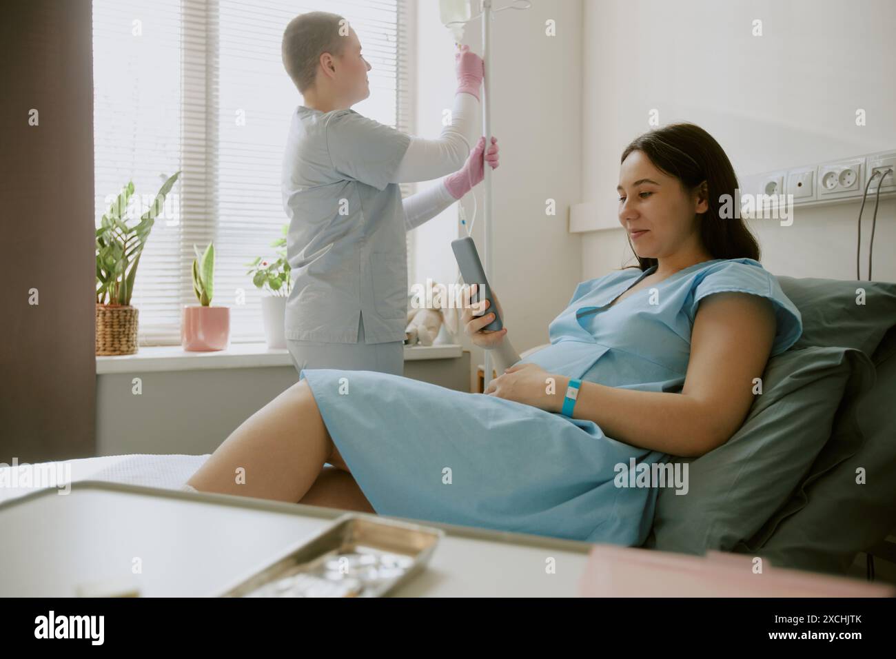 Pregnant patient lying on hospital bed and texting via phone while ...