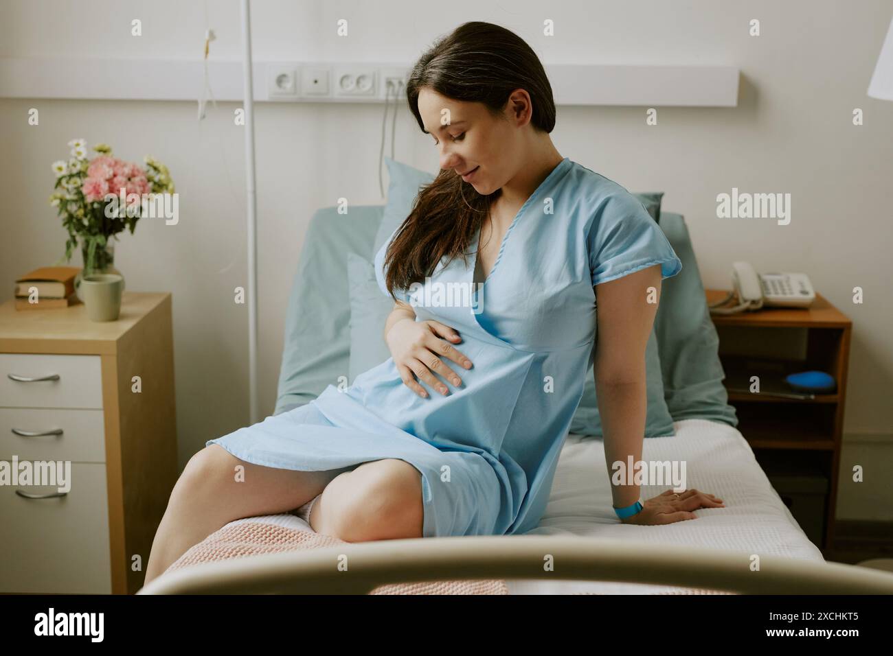 Pregnant patient dressed in light blue nightgown admiring her belly and ...