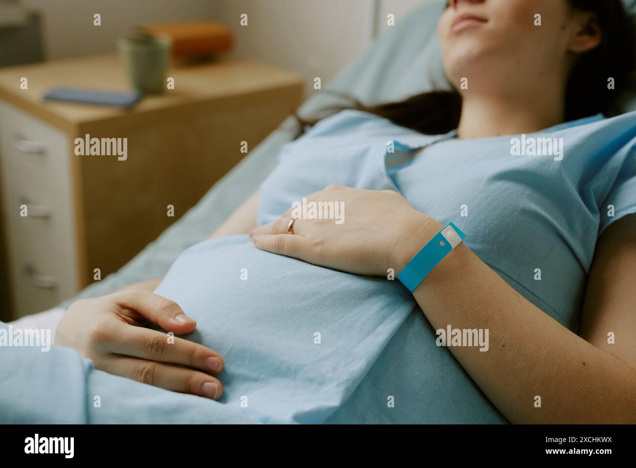 Pregnant patient lying on bed and caressing her tummy while she having ...