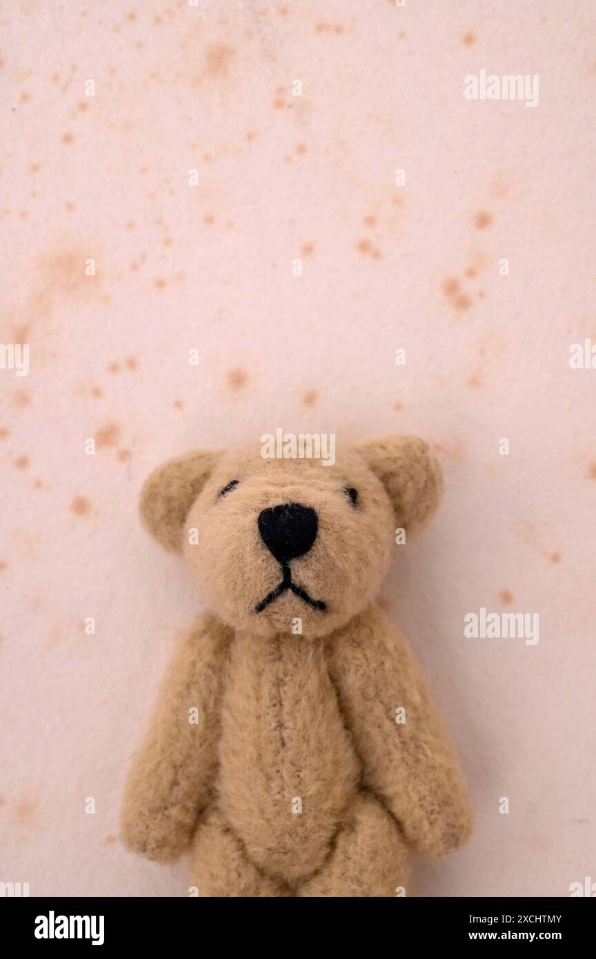 Small beige teddy bear with sad face standing in front of stained wall ...