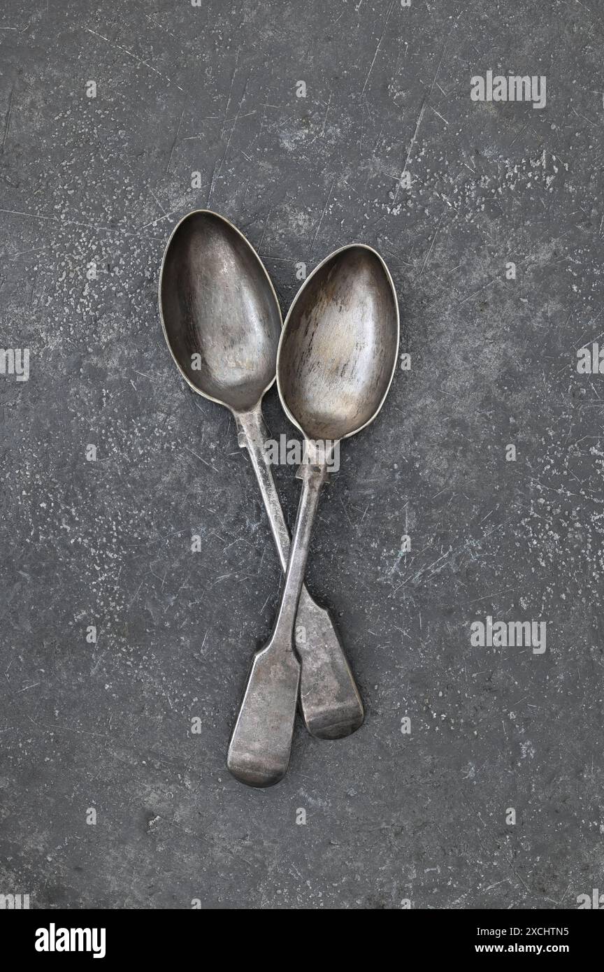 Two tarnished teaspoons lying on scratched pewter Stock Photo - Alamy