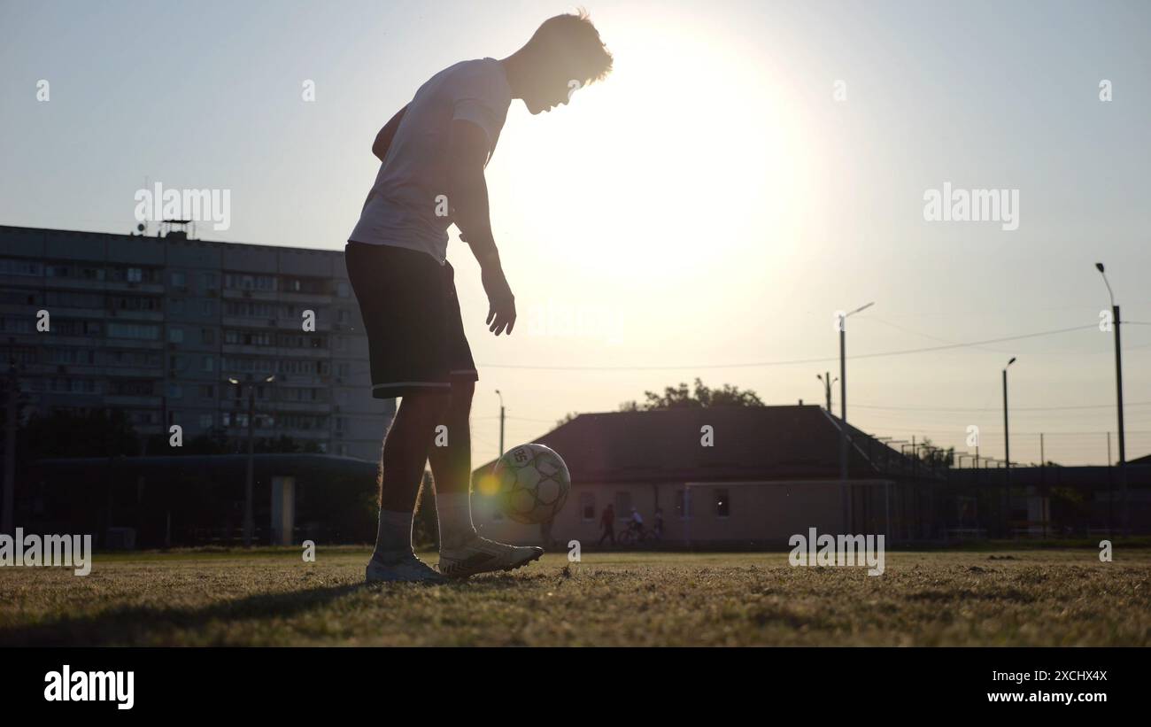 Professional footballer juggling soccer ball on stadium at sunset ...