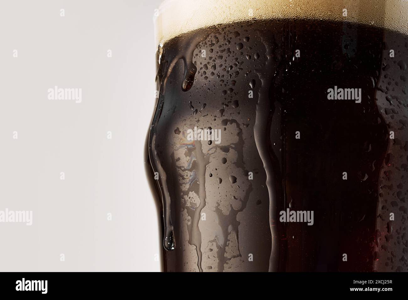 Pint glass filled with dark, cold, foamy craft beer with droplets on ...