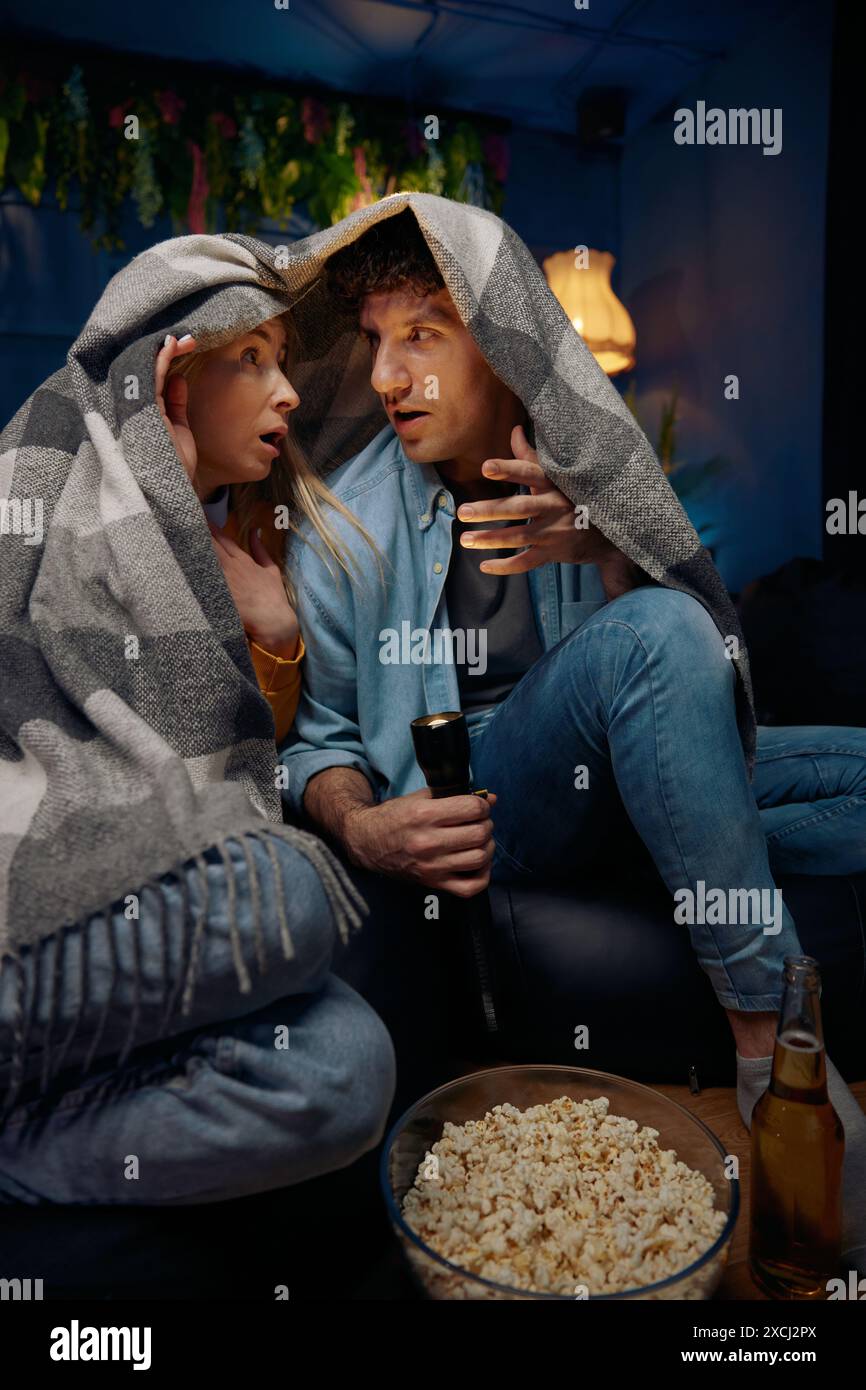 Man tells his girlfriend a scary story using a flashlight and covered ...