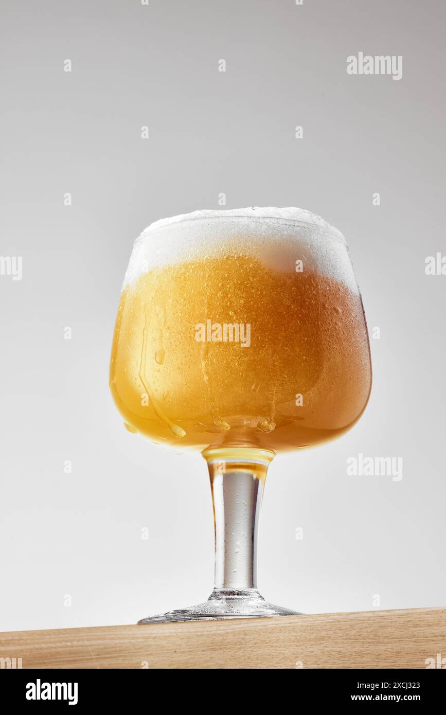 Image of goblet filled with hazy, golden beer topped with thick, creamy ...