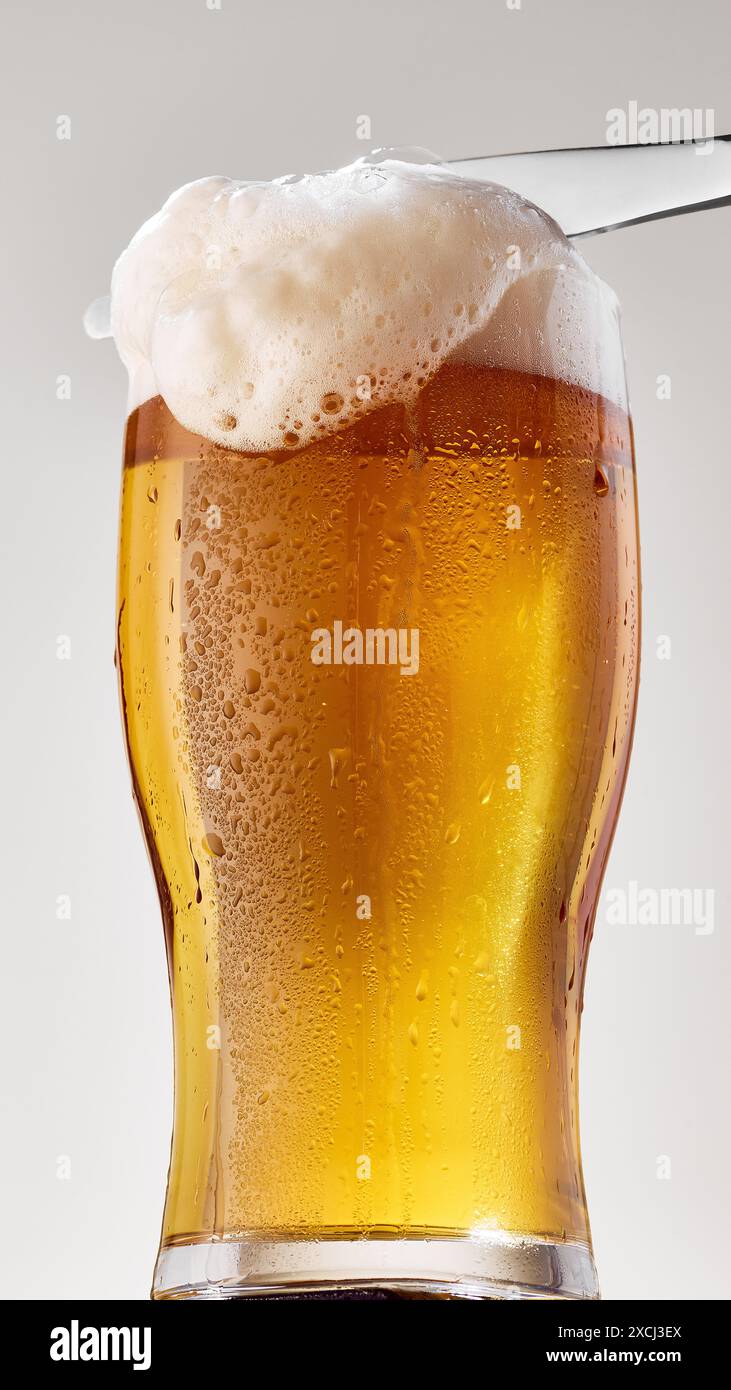 Pint glass filled with bright, golden beer has thick, creamy foam head ...