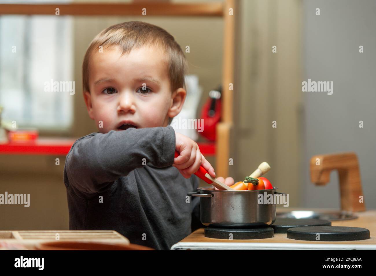 Child playing at cooking by mixing wooden food in metal pot. Symbolic ...