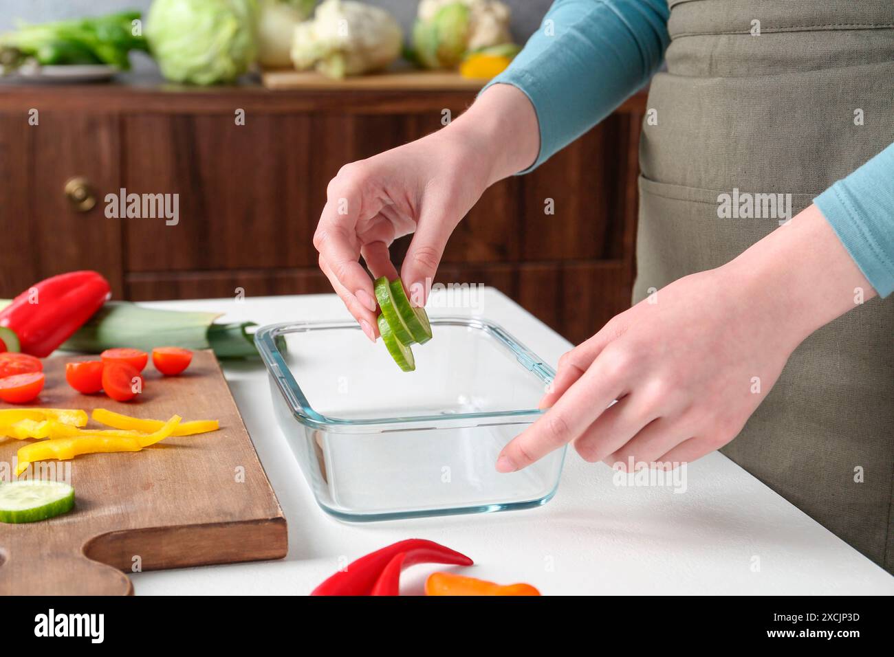 Healthy food. Woman putting slices of cucumber into glass container at ...