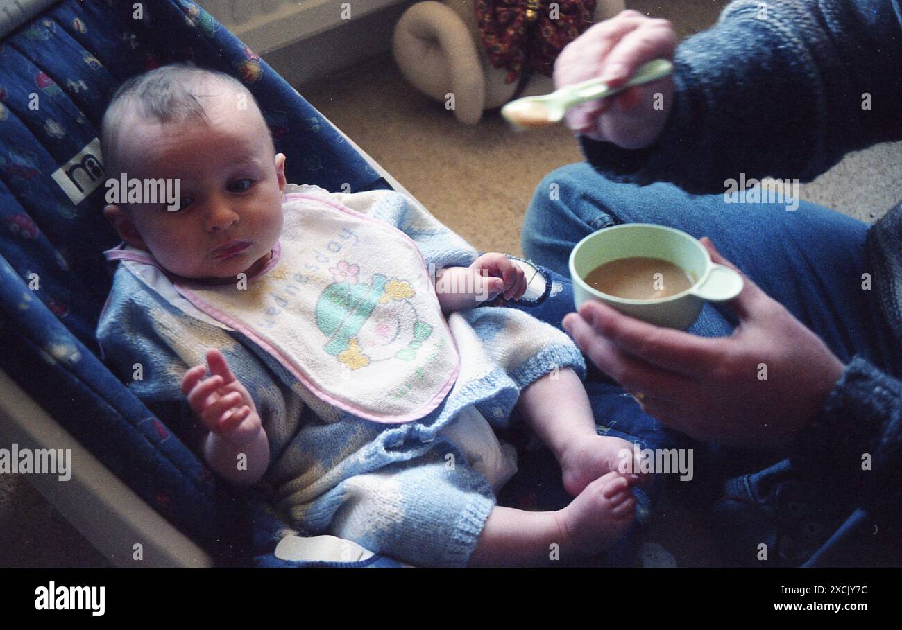 1970s, infant child sitting in a car seat of the era, on the floor ...