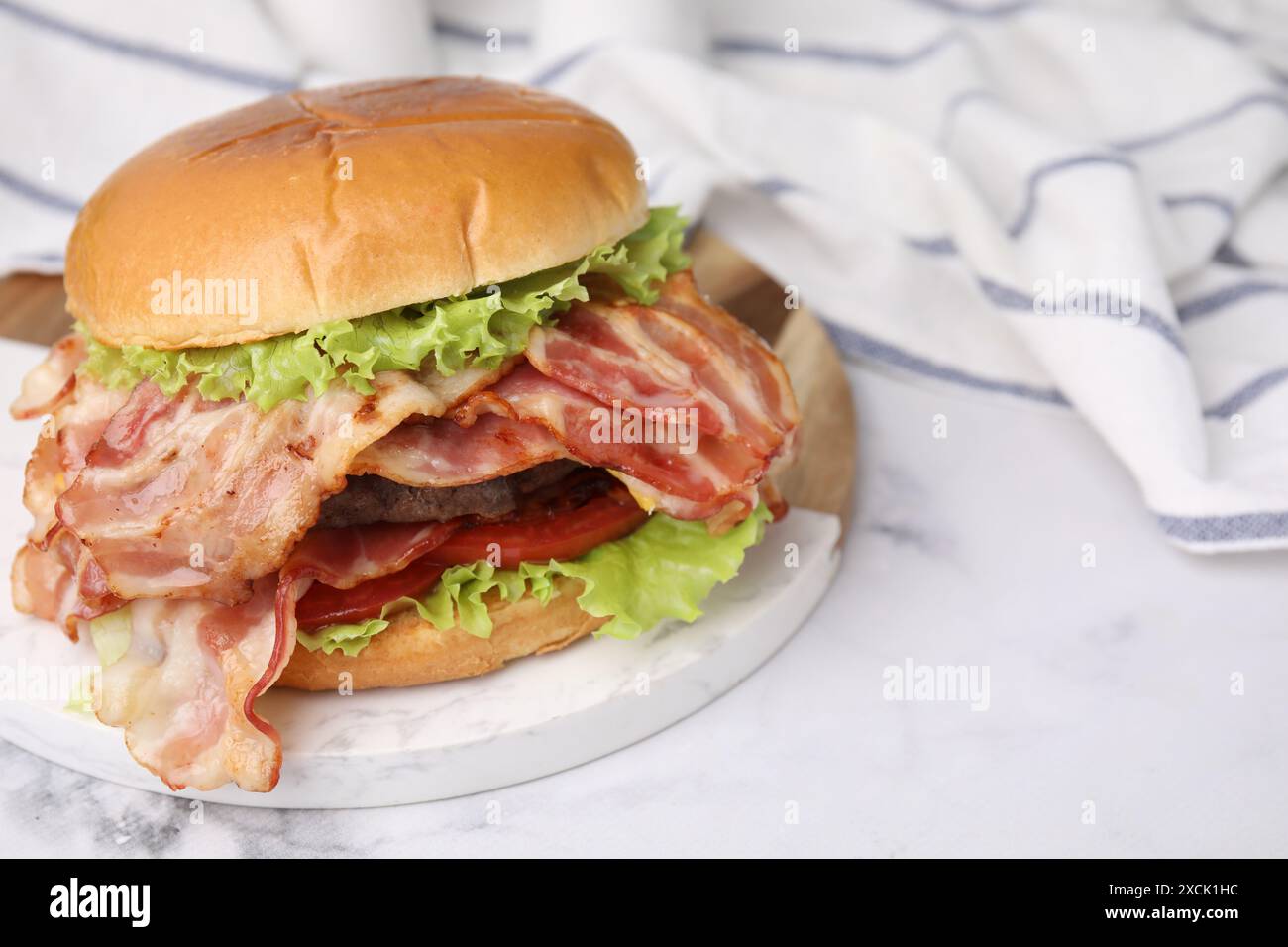 Delicious burger with bacon, patty and tomato on white marble table ...