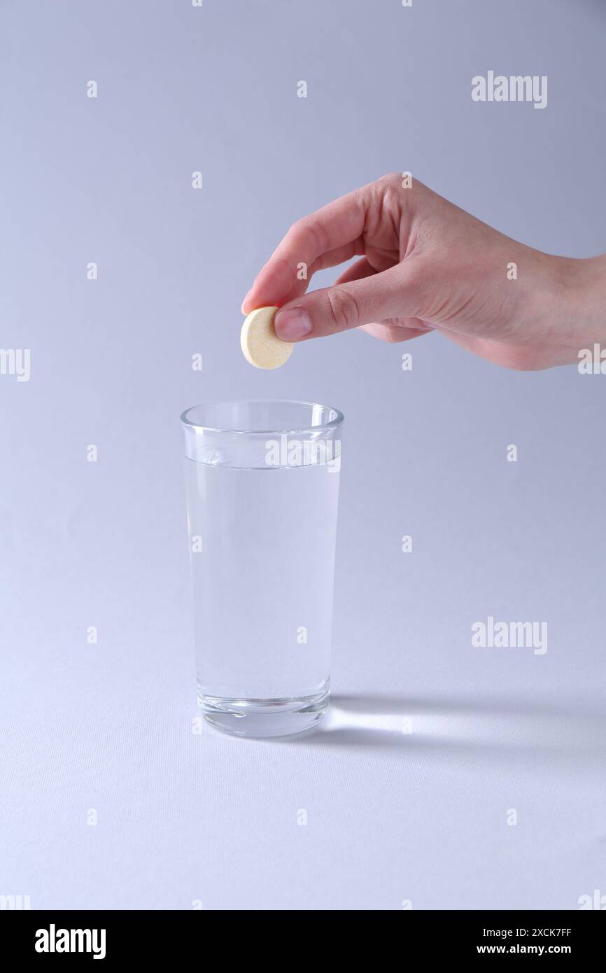 Woman putting effervescent pill into glass of water on light grey ...