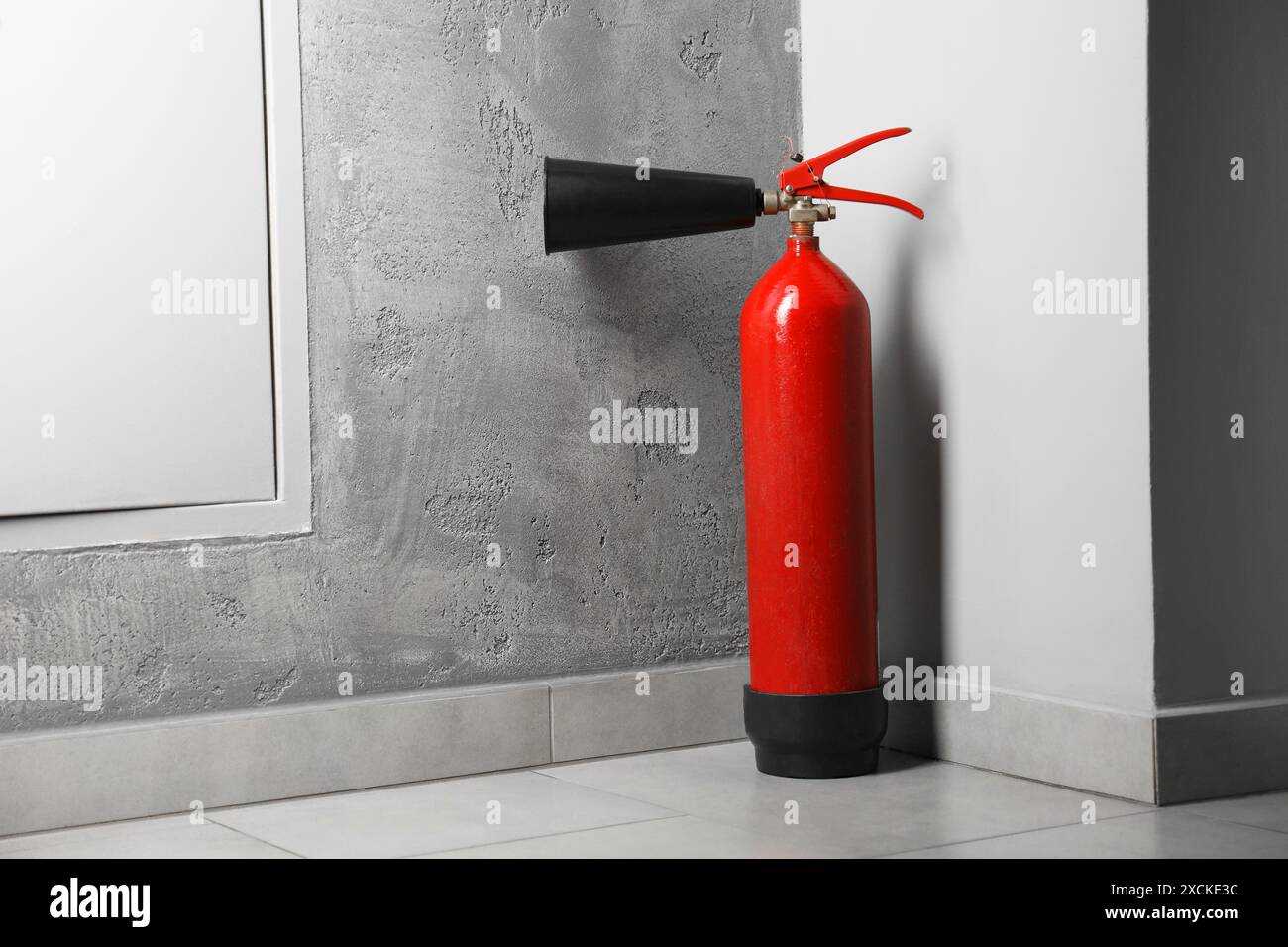 Fire extinguisher on floor near grey wall indoors Stock Photo - Alamy