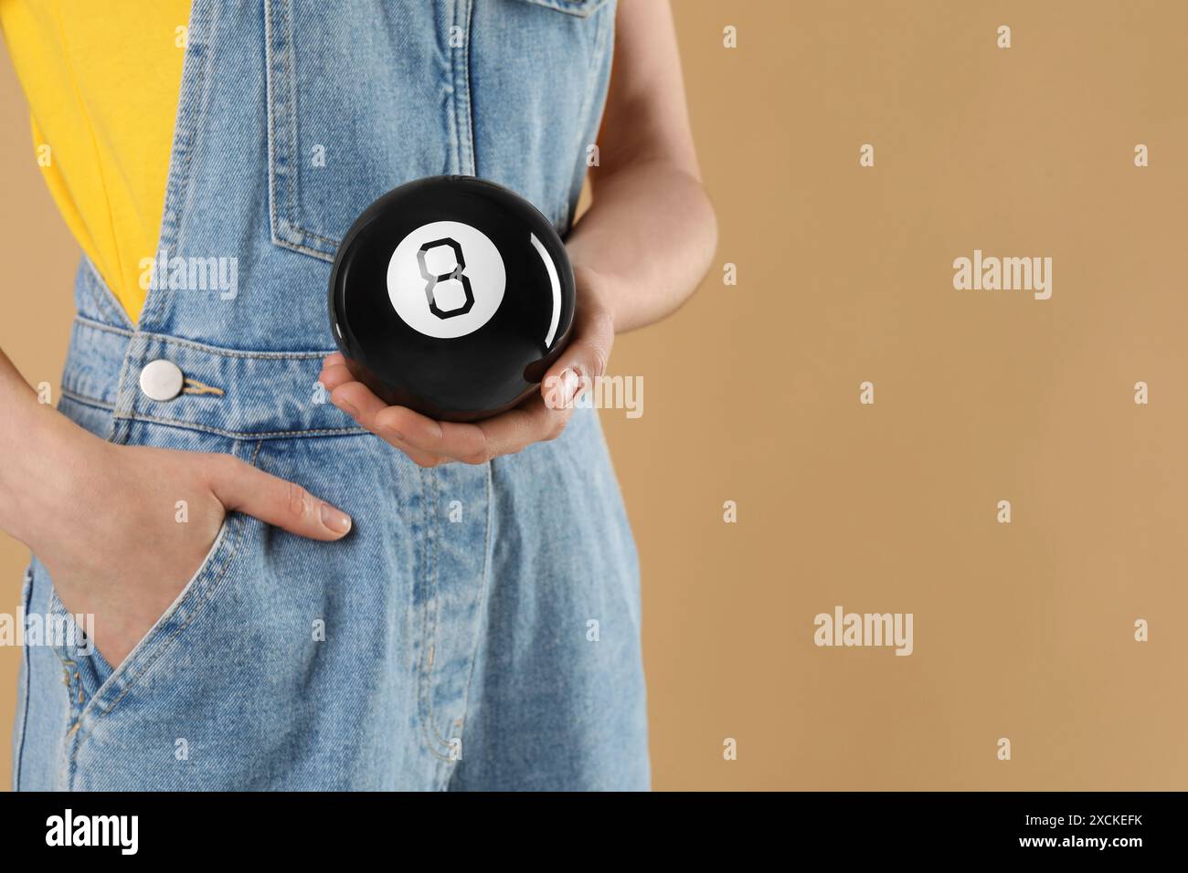 Woman holding magic eight ball on light brown background, closeup ...