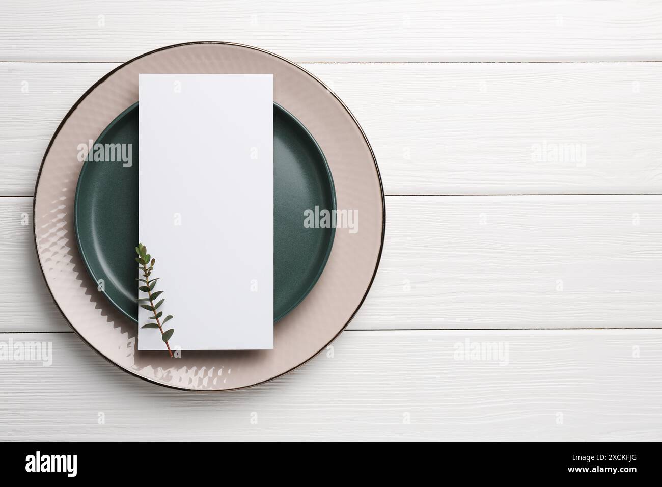 Empty menu, plates and floral decor on white wooden table, top view ...