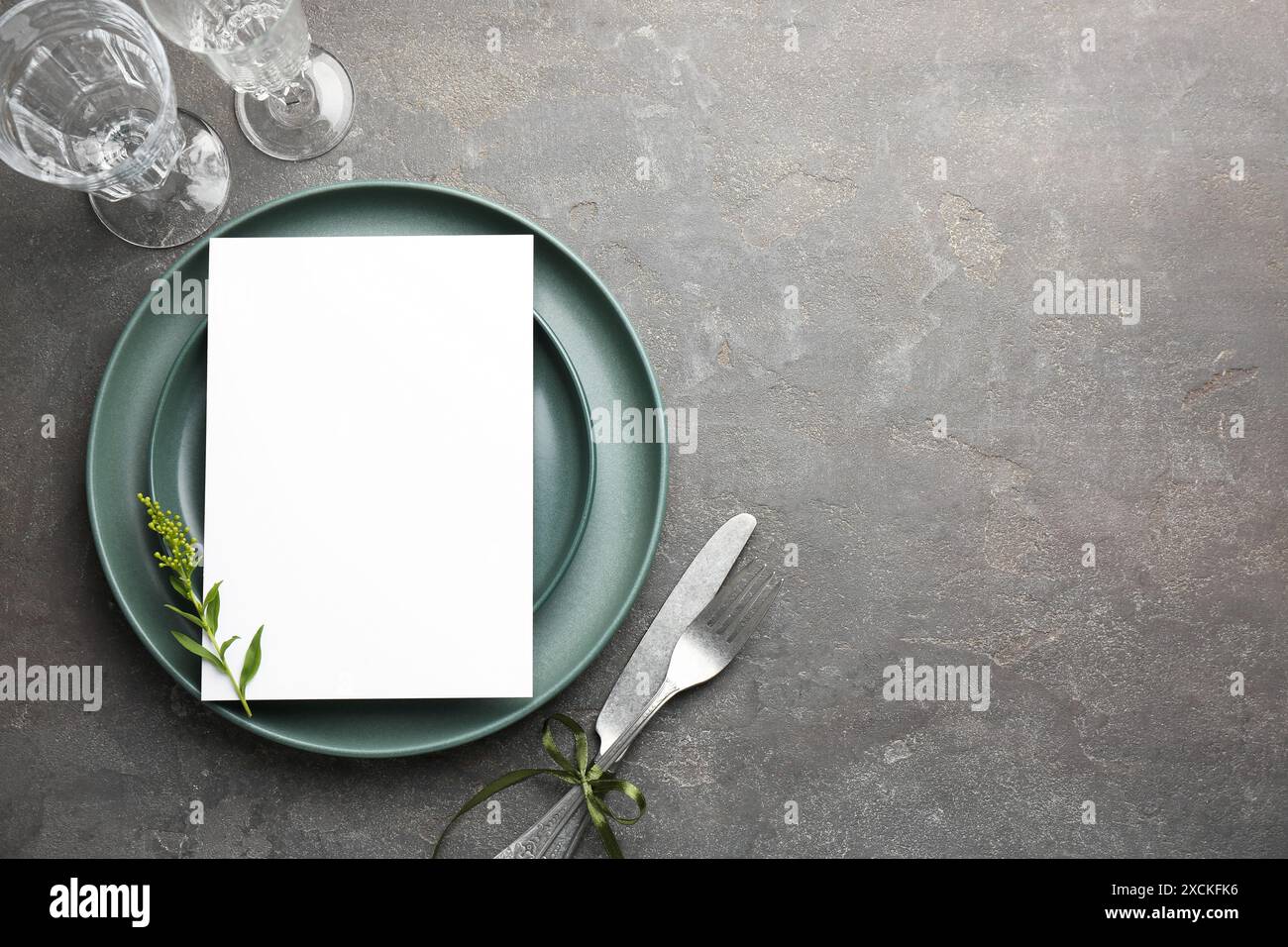 Empty menu, plates, cutlery, glasses and floral decor on grey table ...