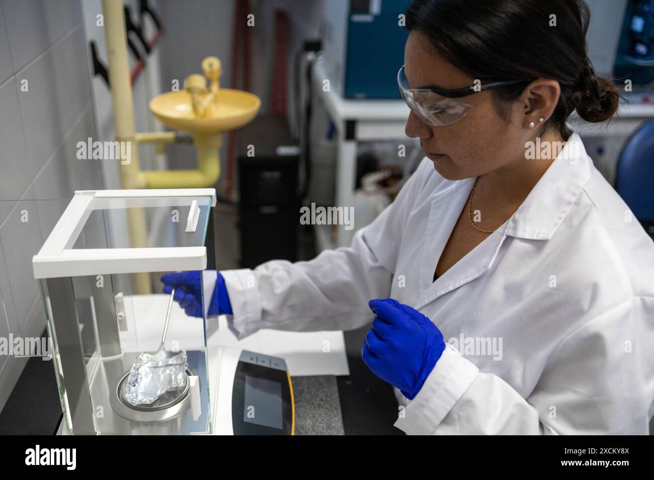 side-view of a woman scientist weighing a solid white sample on a scale ...