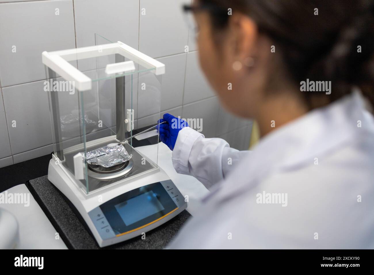 back-view of a woman scientist weighing a solid white sample on a scale ...