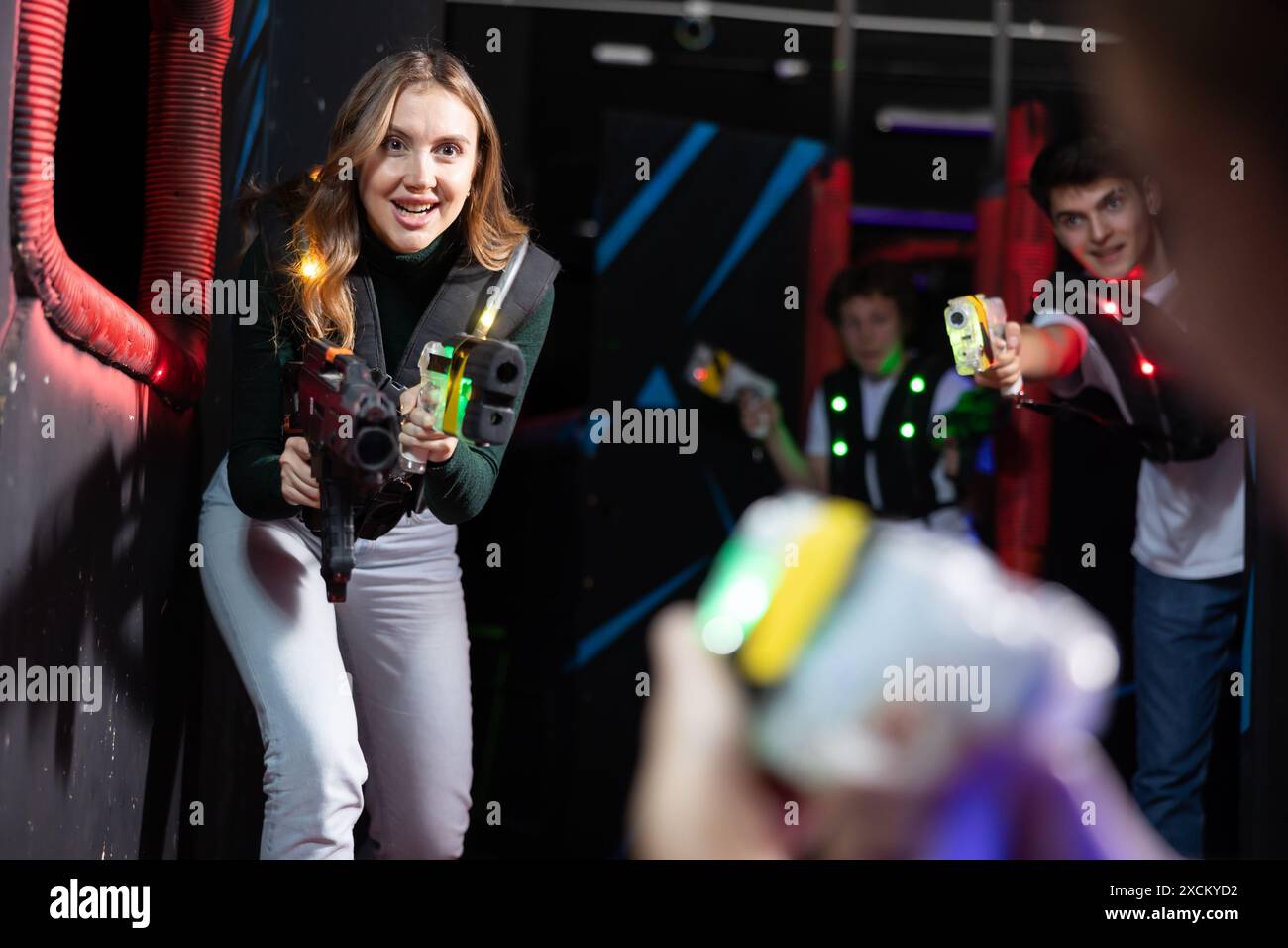 Positive girl holding laser pistol playing laser tag game with friends ...