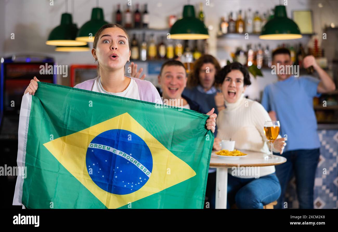 Company of enthusiastic young adult sports fans waving flag of Brazil ...