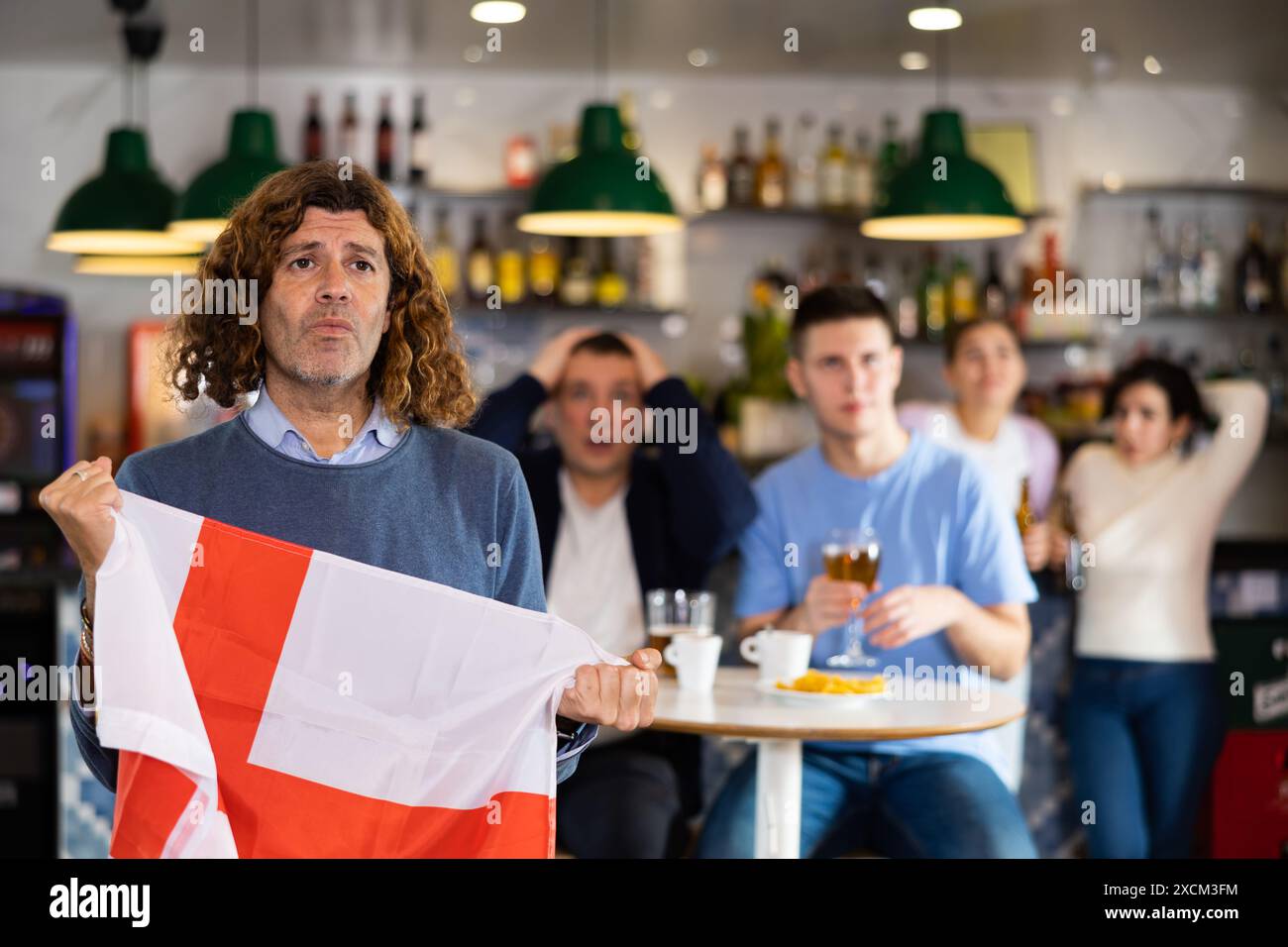 Company of upset young adult sports fans holding flag of England and ...