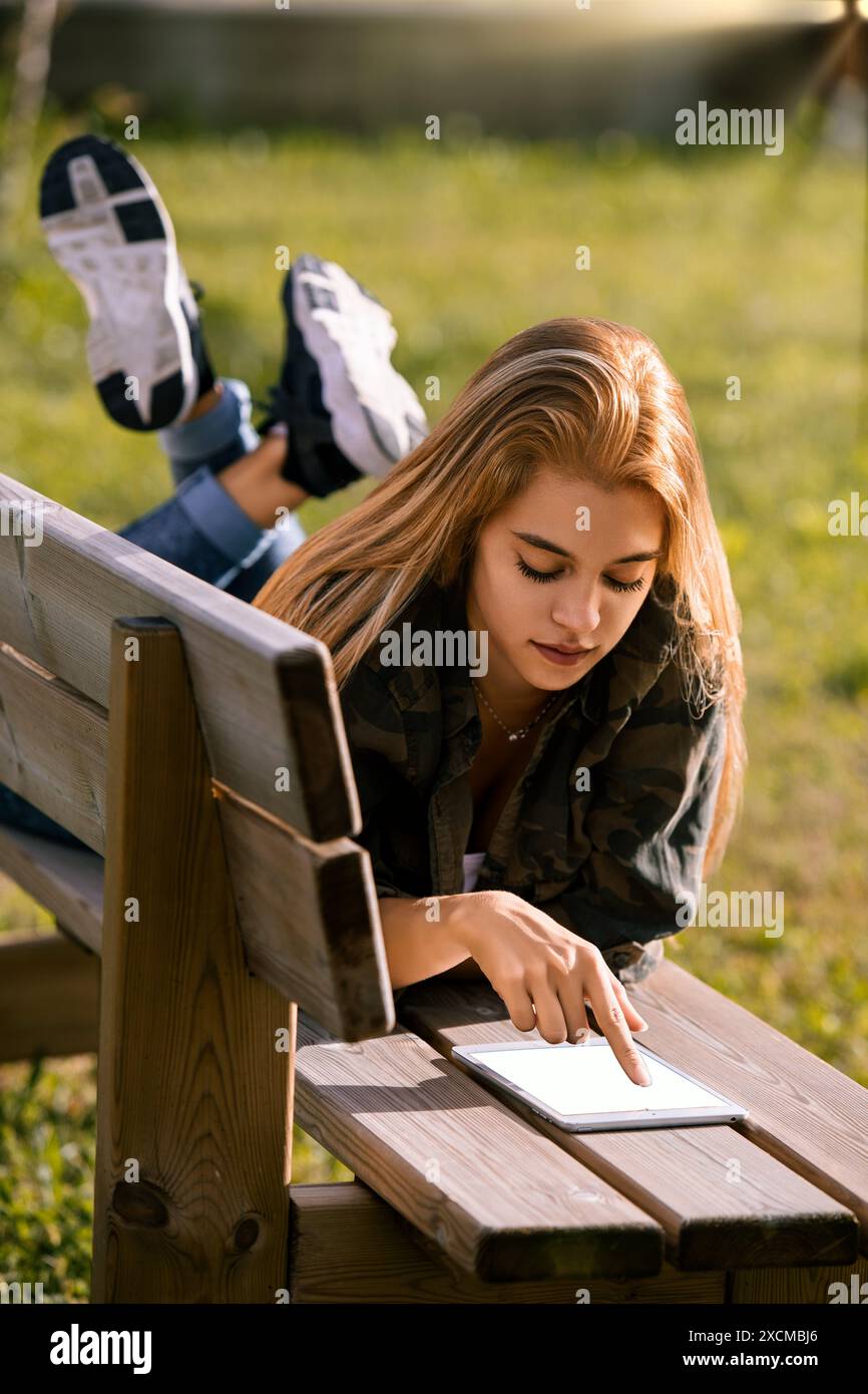 Young woman is using a digital tablet while laying on her stomach on a ...