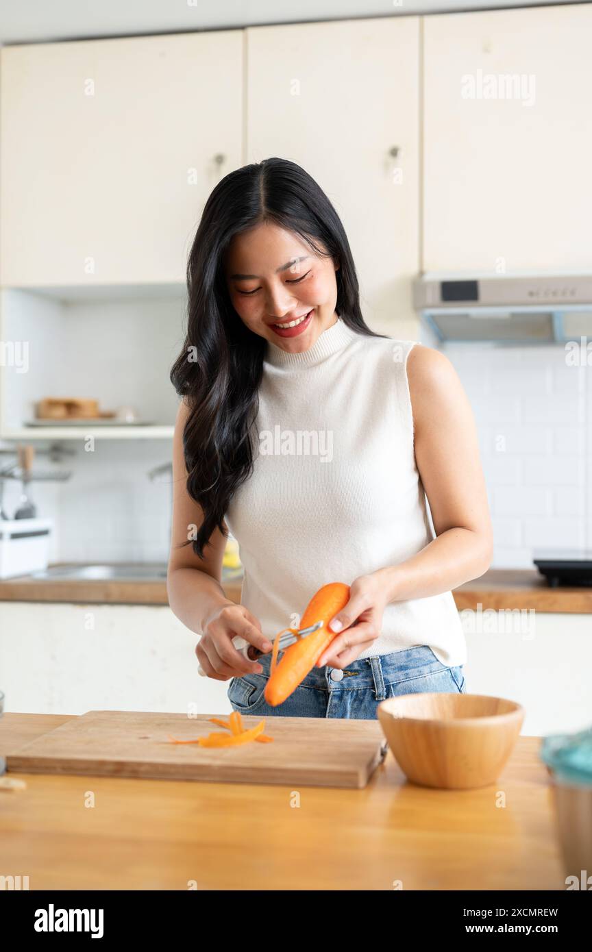 An attractive, charming Asian woman cooking in the kitchen, peeling a ...
