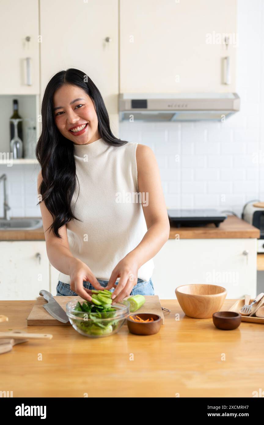 An attractive, positive young Asian woman enjoying cooking in the ...