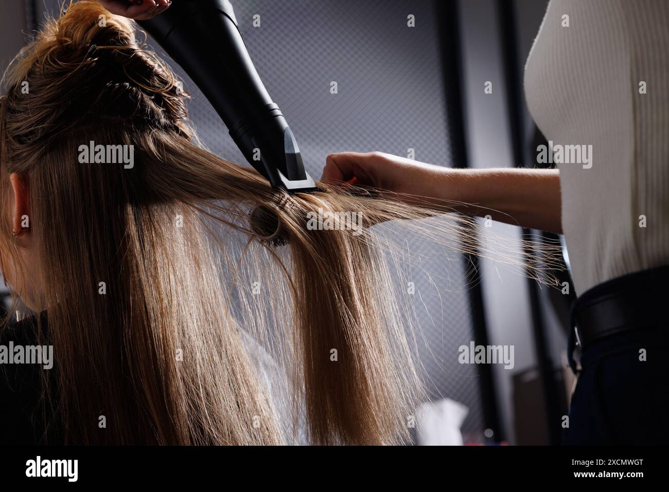 hairdresser drying hair with hair dryer and comb in beauty salon ...
