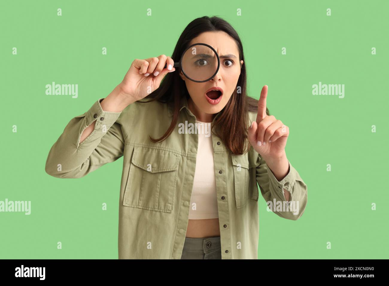 Shocked young woman with magnifier pointing at something on green ...