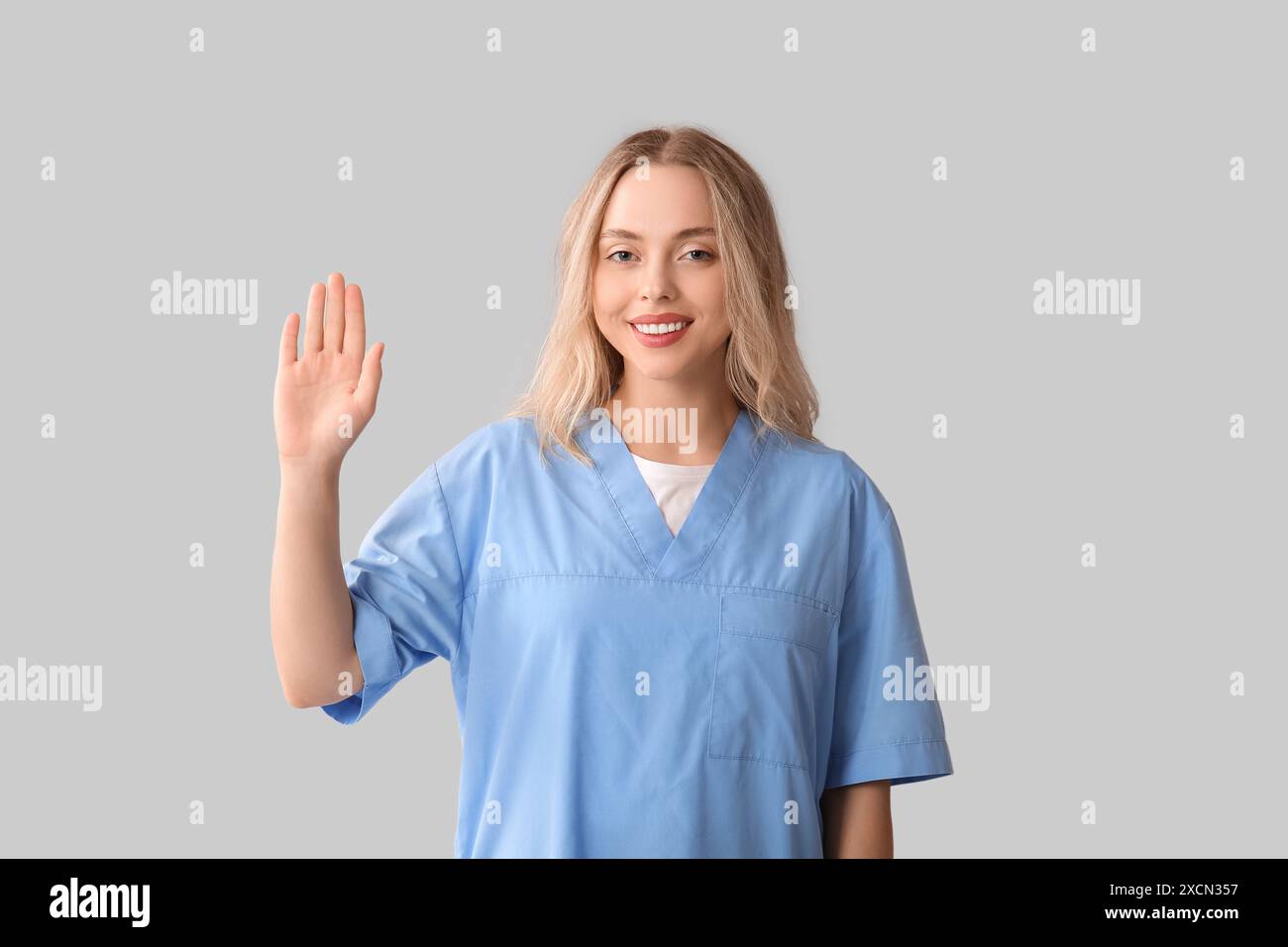 Beautiful female doctor waving hand on grey background Stock Photo - Alamy