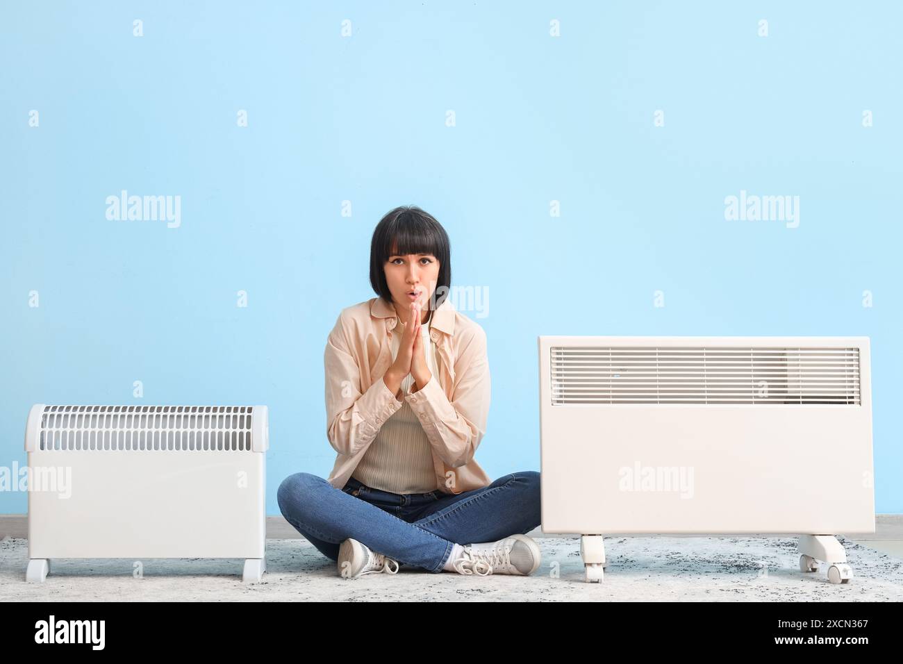 Frozen young woman with radiators sitting near blue wall Stock Photo ...