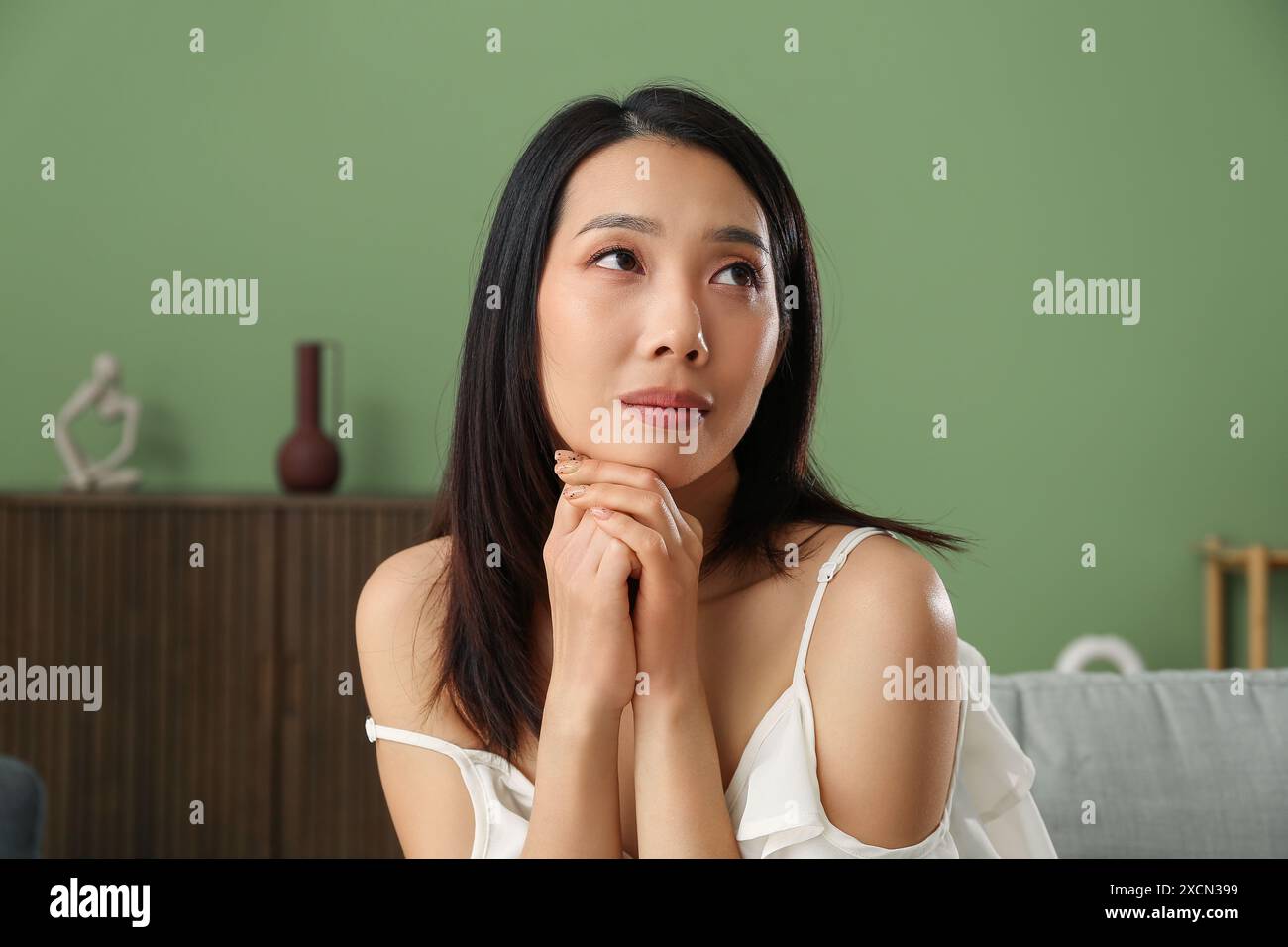Portrait of thoughtful young Asian woman in living room Stock Photo - Alamy