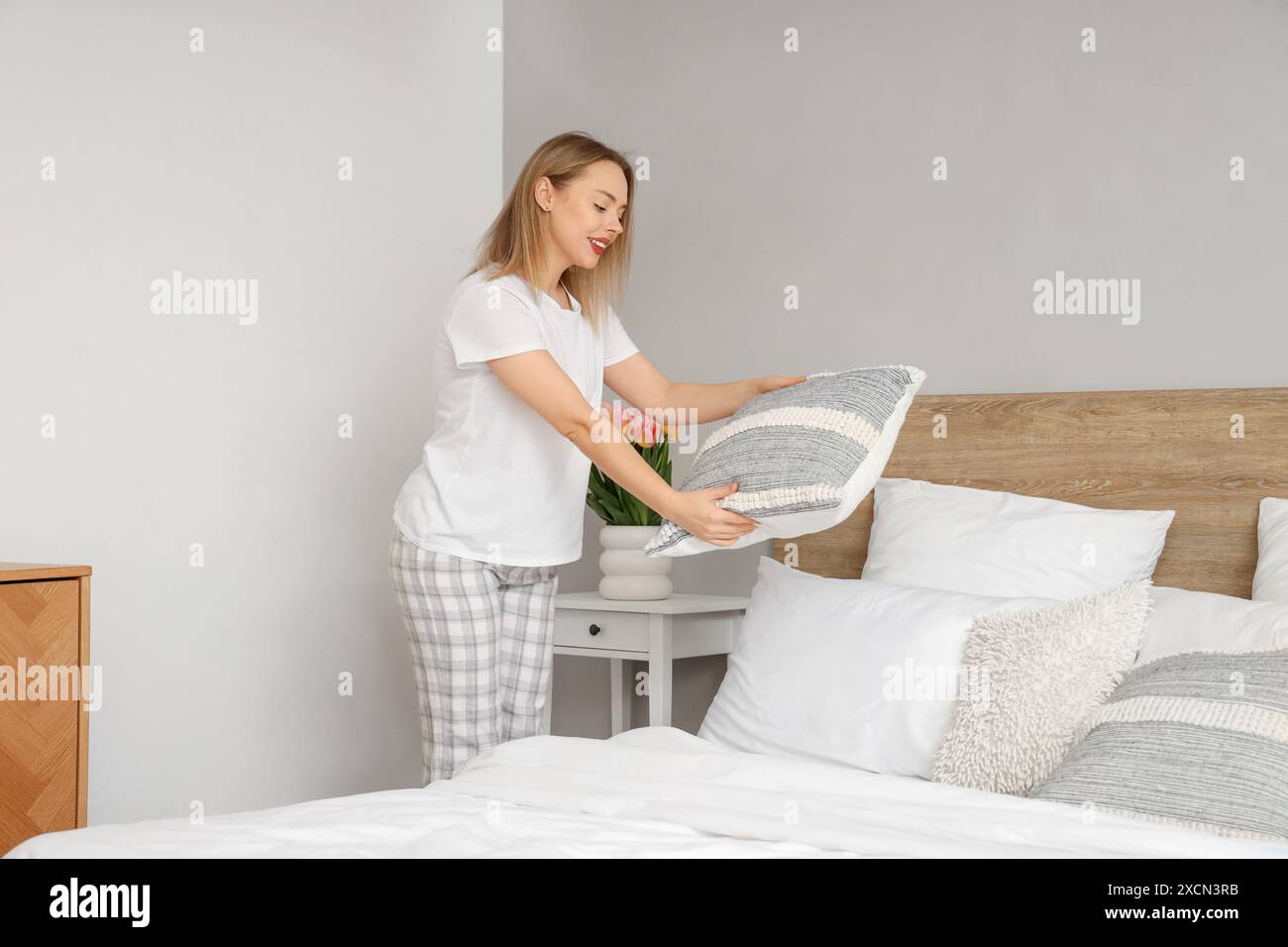 Pretty young woman making bed in bedroom Stock Photo - Alamy