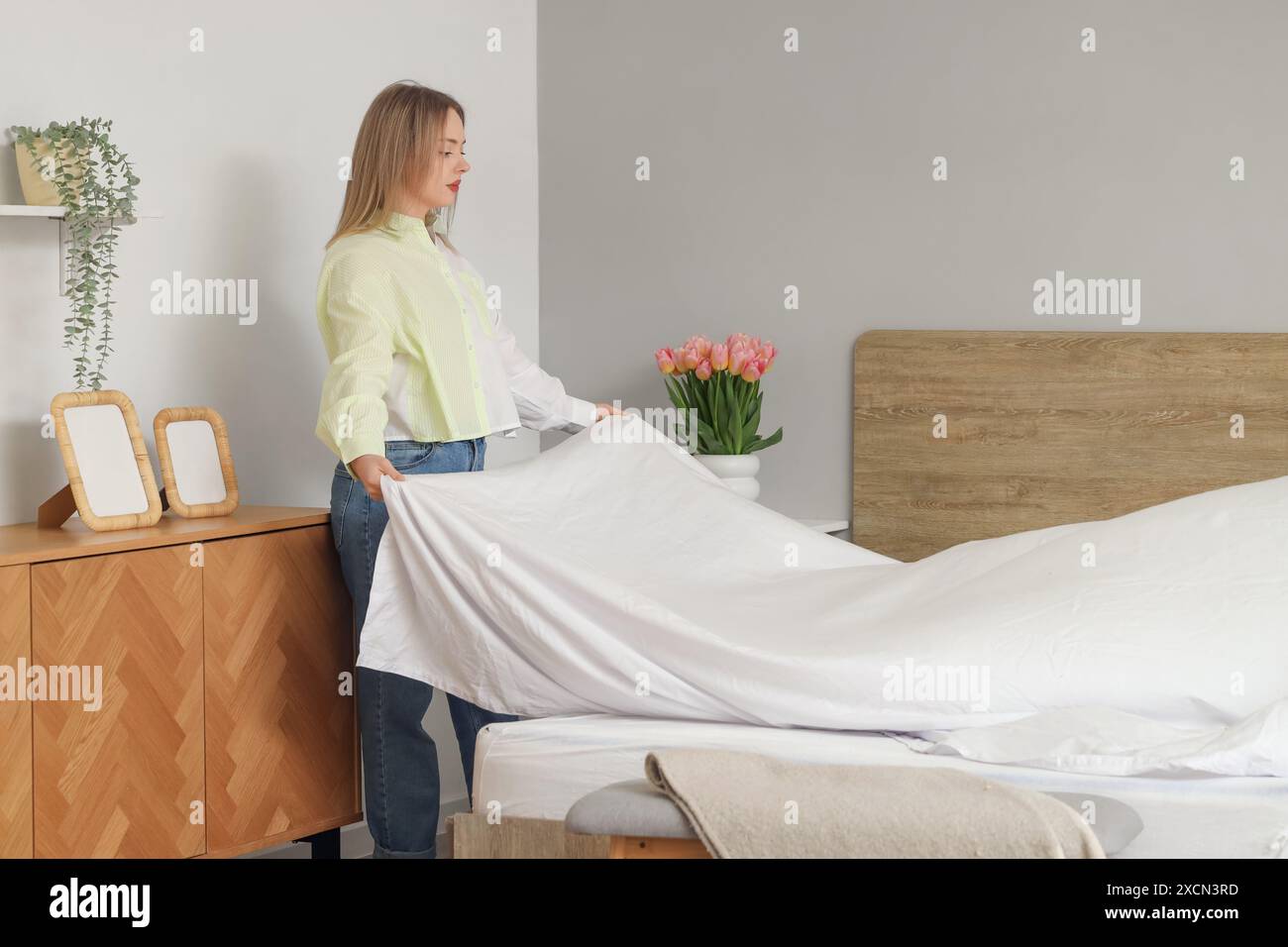 Pretty young woman making bed in bedroom Stock Photo - Alamy