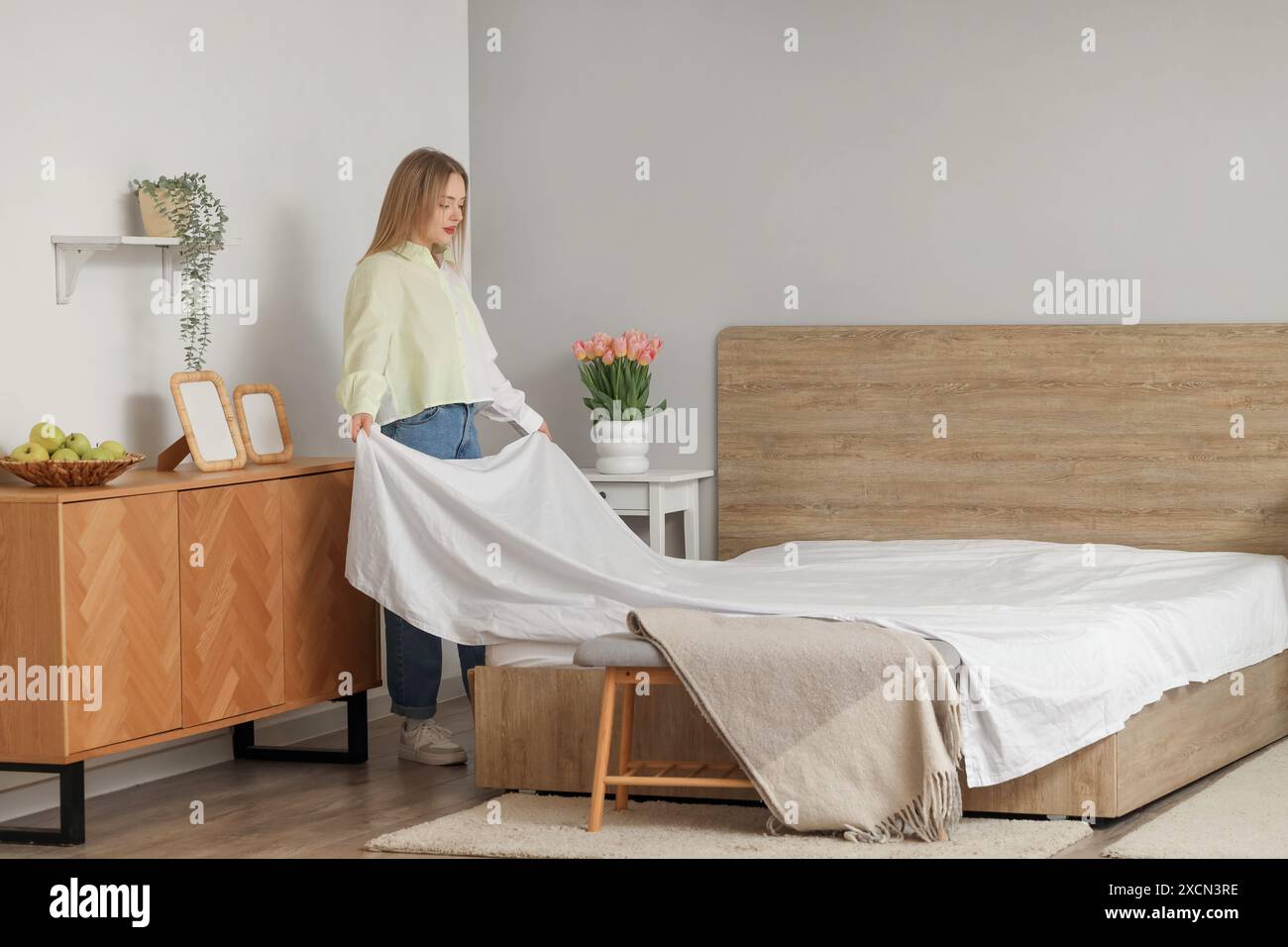Pretty young woman making bed in bedroom Stock Photo - Alamy