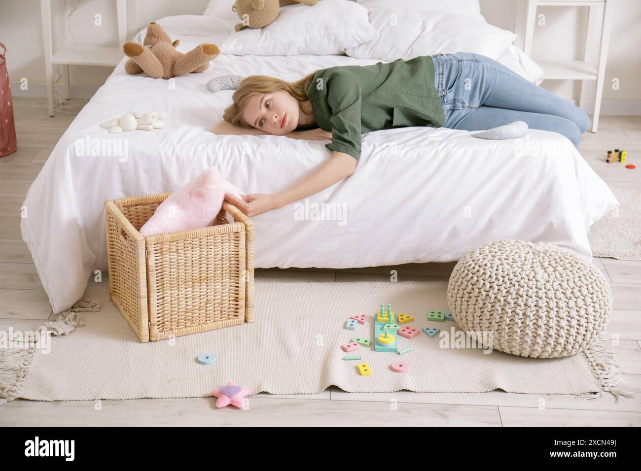 Tired young mother resting in bedroom with scattered toys on floor ...
