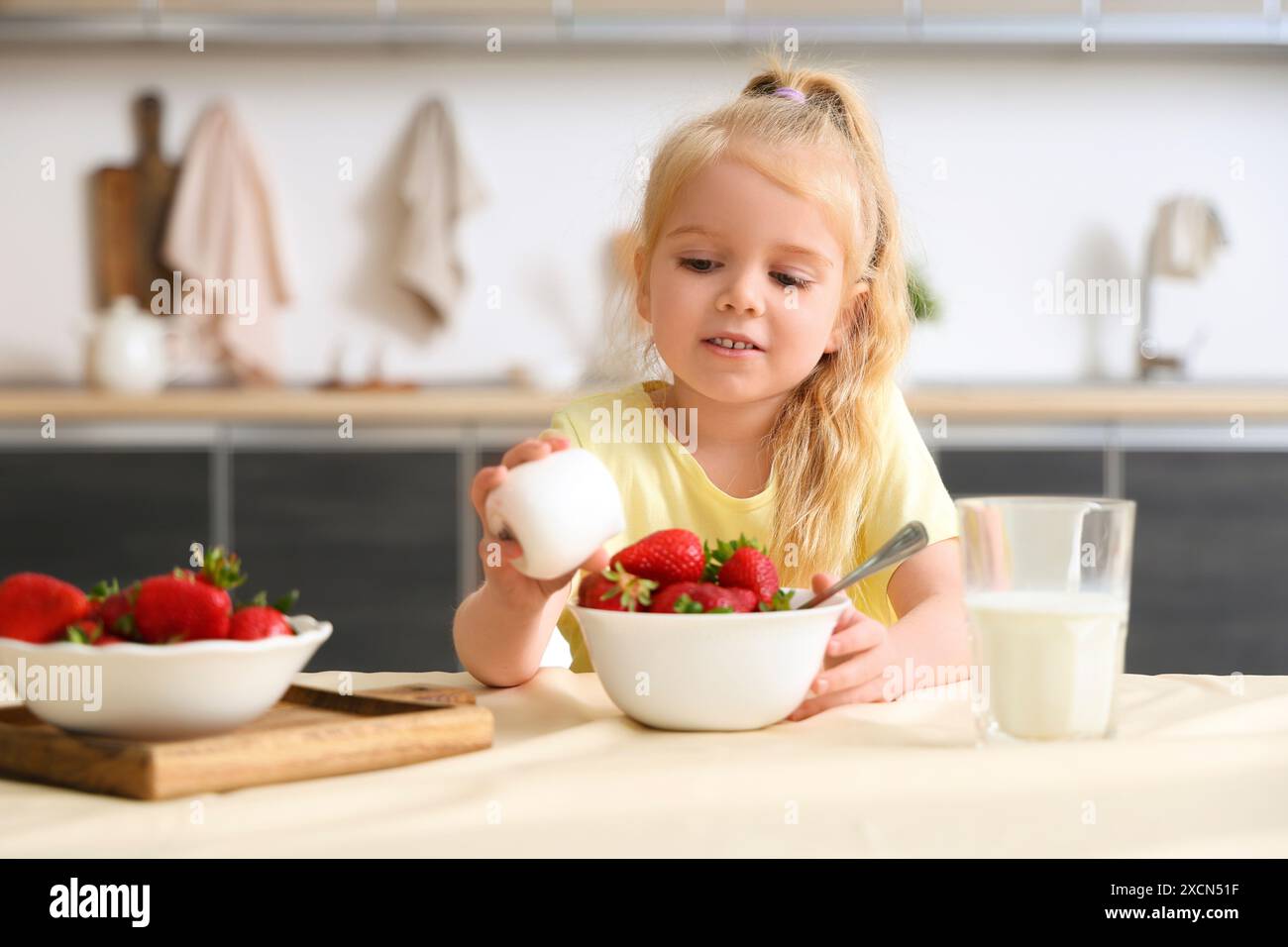 Little girl pouring cream in bowl of strawberries in kitchen Stock ...