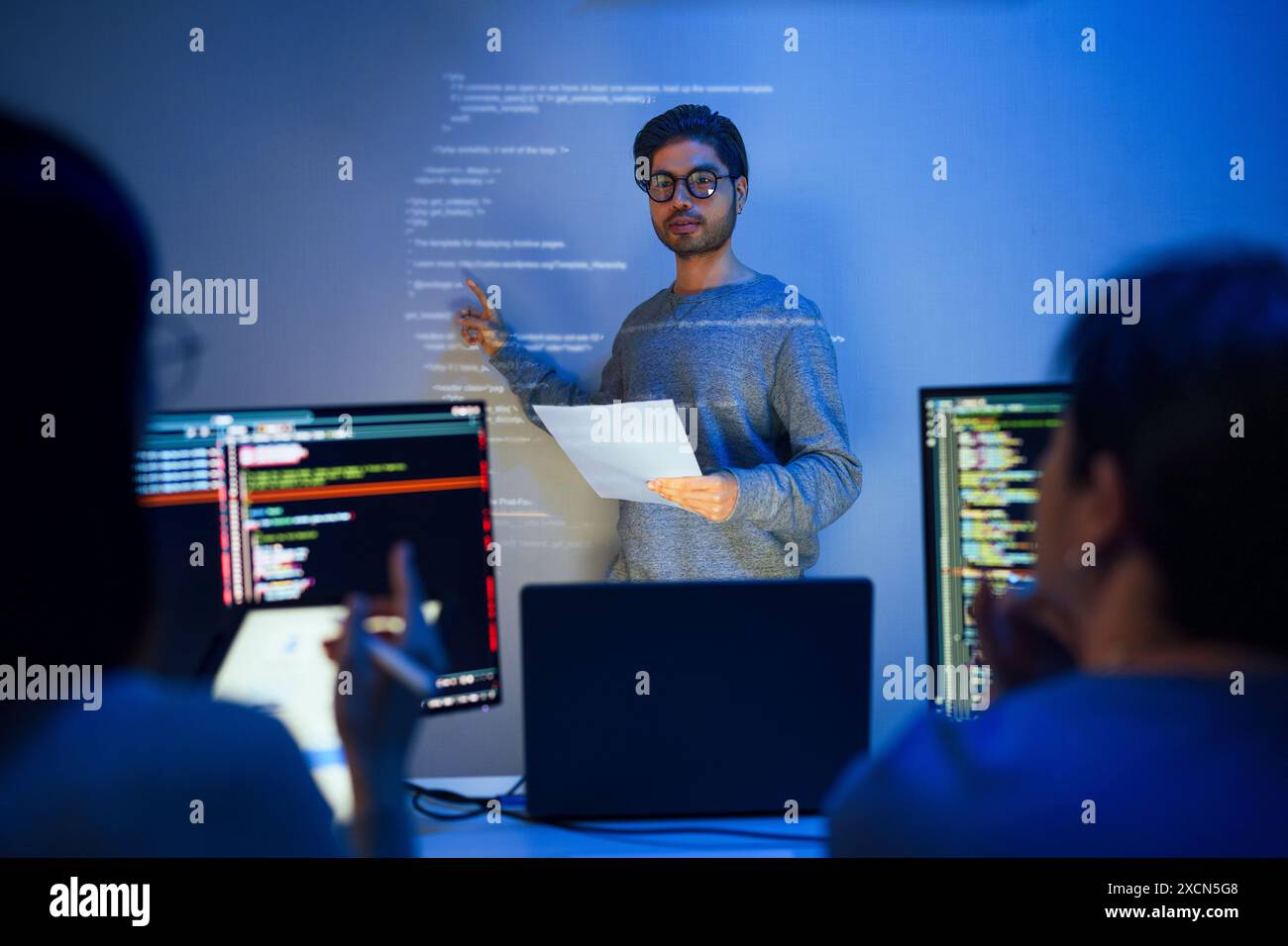 asian developer leads present code review session, pointing at code projected on the wall with ...