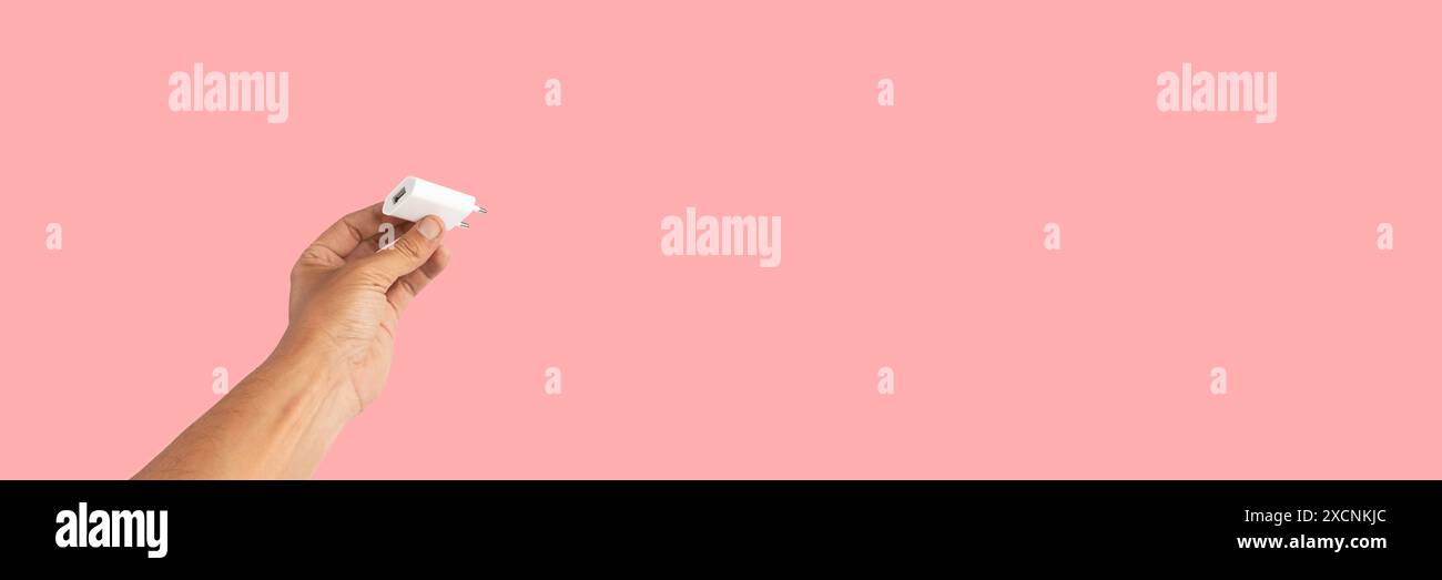 Black male hand holding a USB charger plug isolated on pink background ...