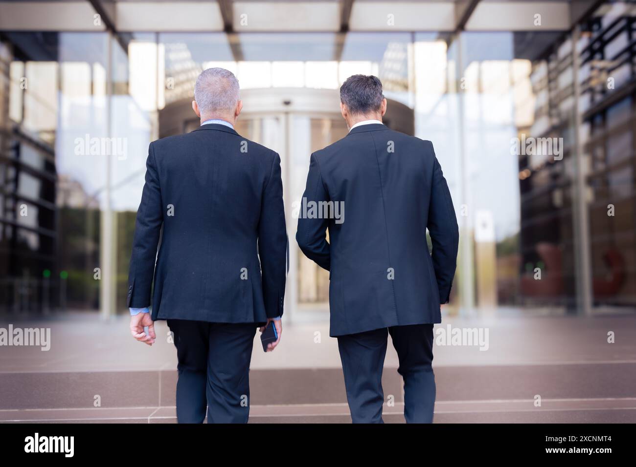 Rear view of two businessmen walking to enter office building outdoors ...