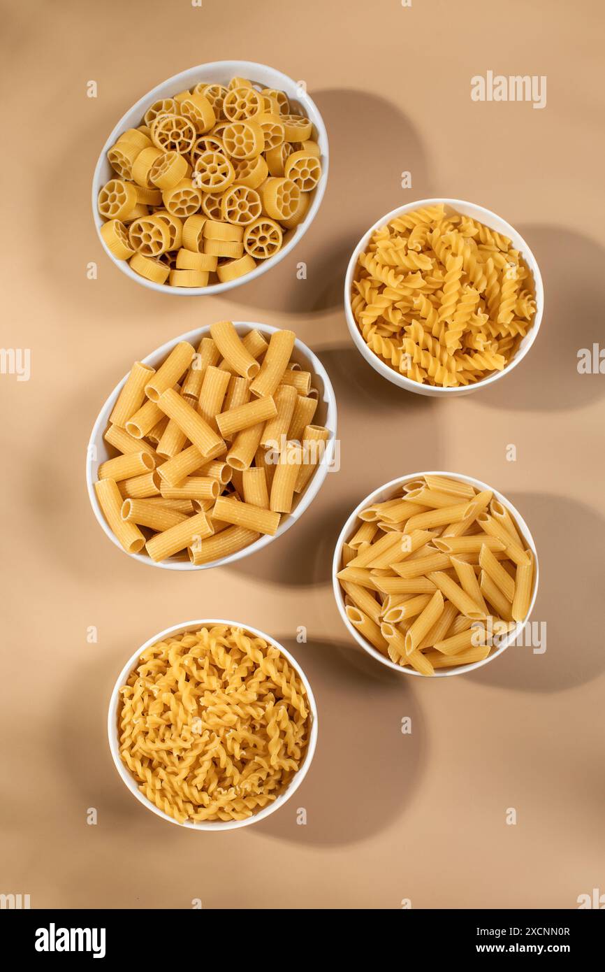 Raw pasta variety in bowls on brown background upper view Stock Photo ...