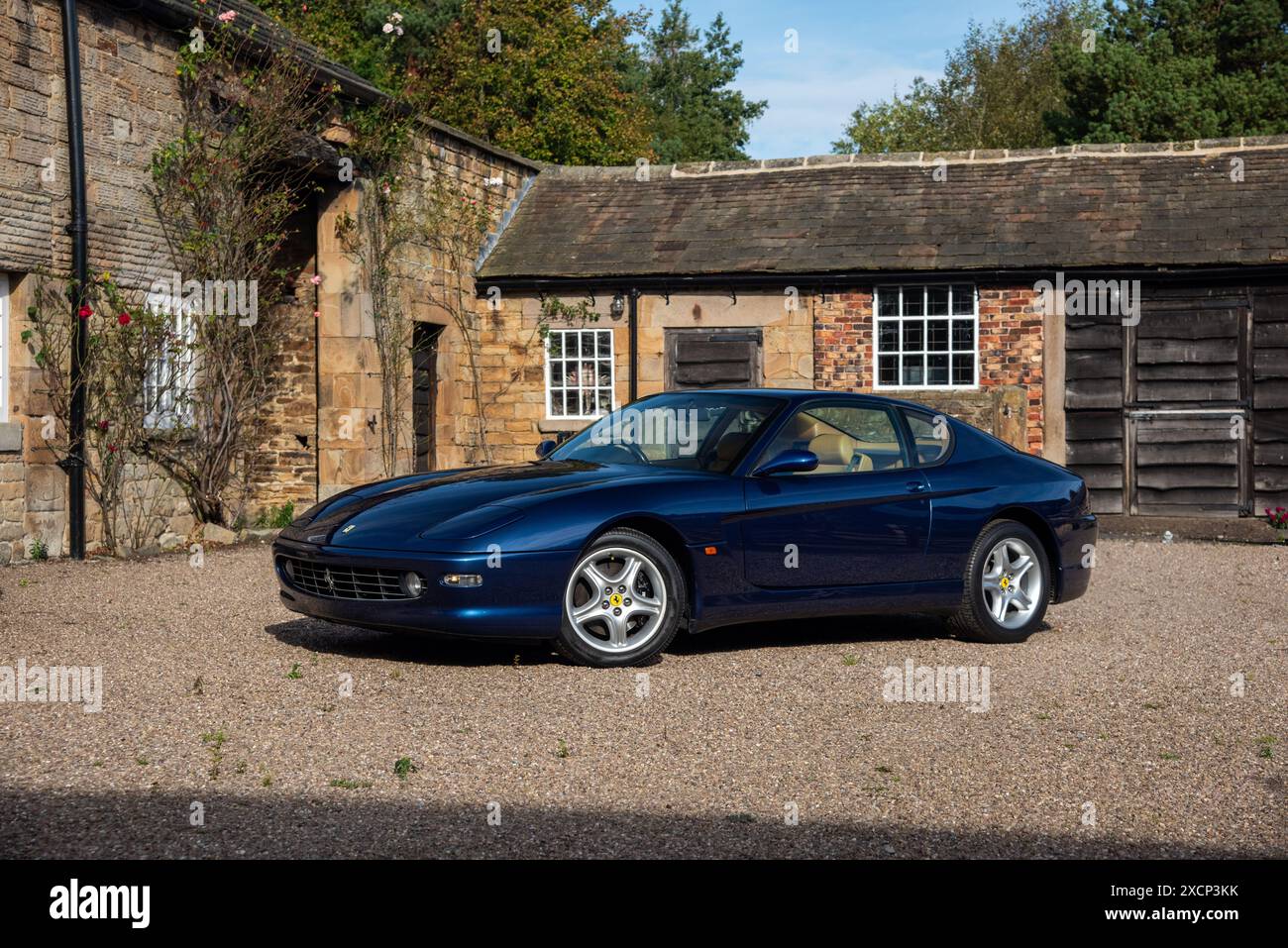 Blue Ferrari 456 parked on a gravel paddock on a sunny day with stables ...