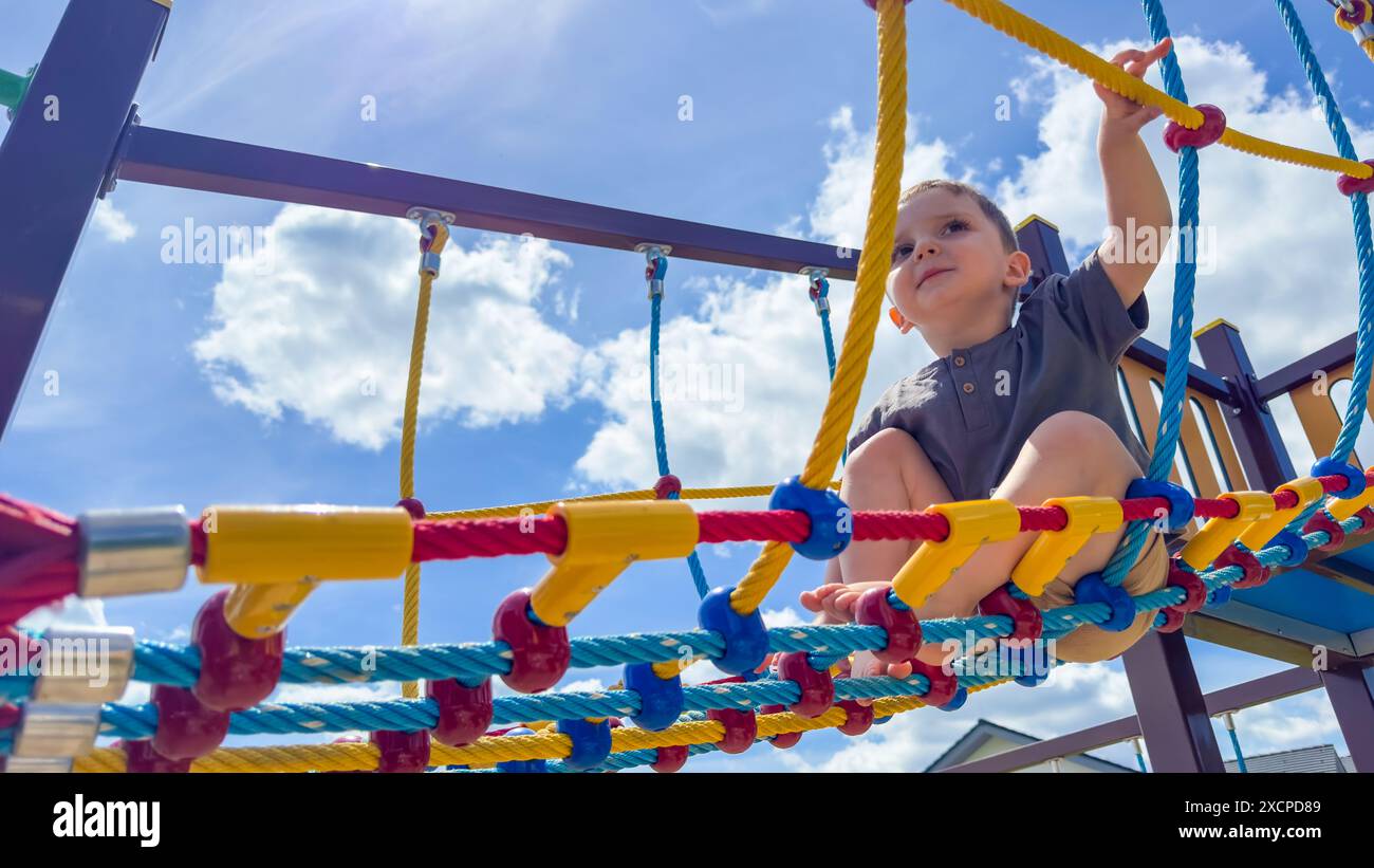 View from the ground on toddler boy walking over the rope bridge at ...