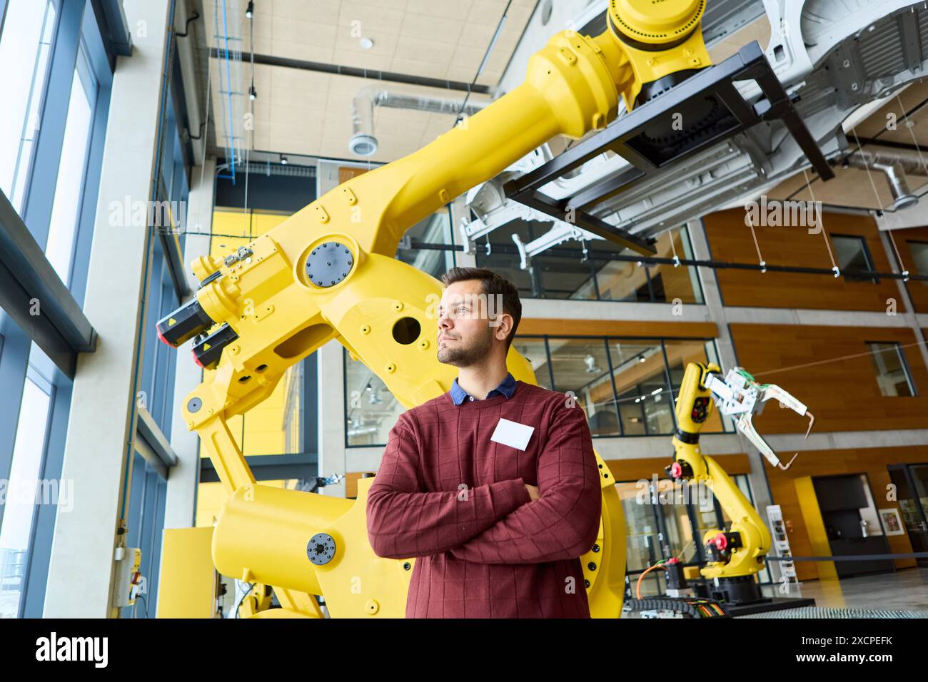 Confident engineer standing with crossed arms in front of a large robotic arm in a modern ...