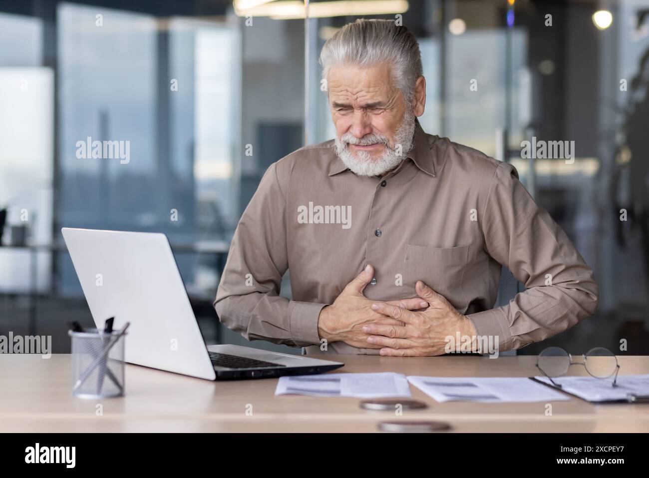 Elderly man experiencing stomach pain while working at a laptop in a ...